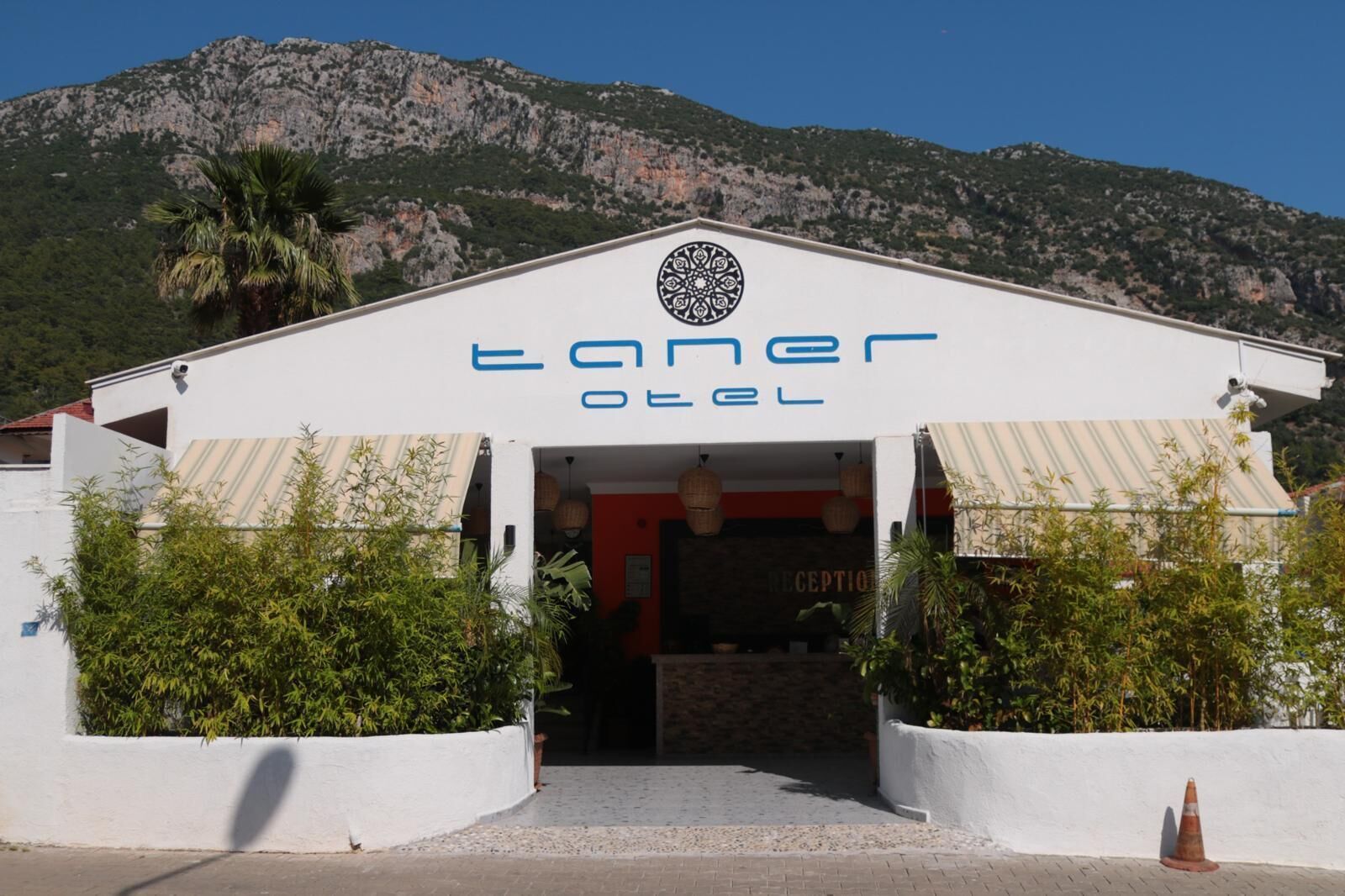 Entrada de hotel com montanhas ao fundo, área de recepção e logotipo acima do nome.