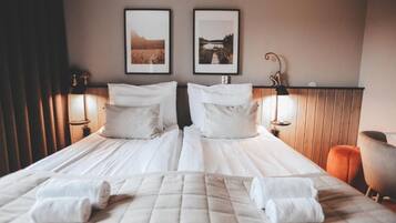 Uma cama de casal com lençóis brancos e duas almofadas, uma mesa de cabeceira com abajur e duas quadros decorativos na parede.