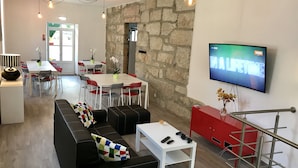 Uma sala de estar moderna com parede de pedra, televisão de tela plana, sofá, área de jantar com cadeiras e uma pequena mesa com controles remotos.