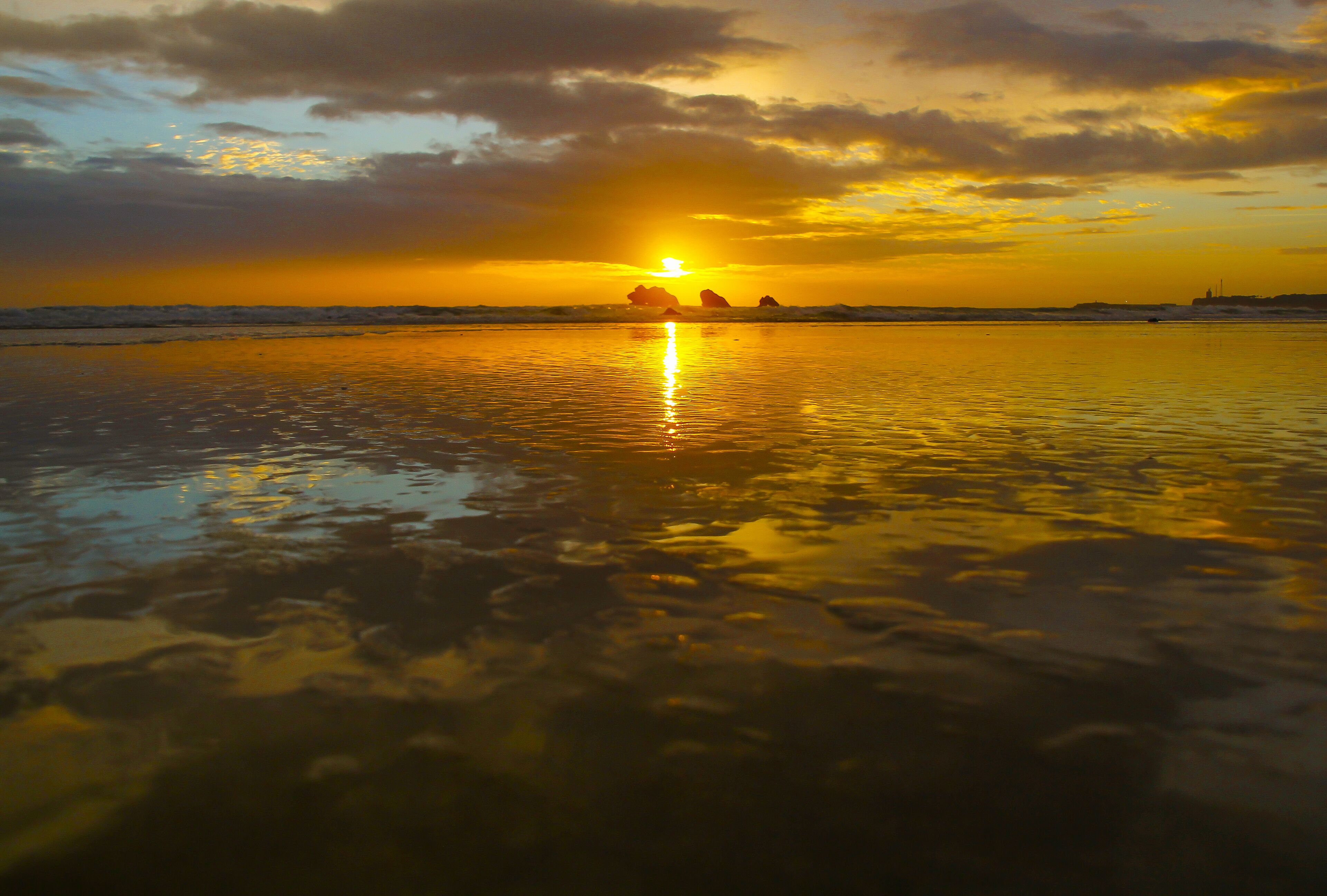 Um pôr do sol sobre uma praia com águas calmas refletindo o céu.