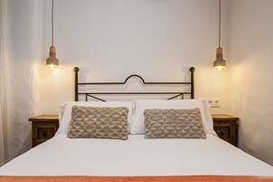 Cama bem arrumada com almofadas estampadas, duas mesas de cabeceira e luminárias pendentes.