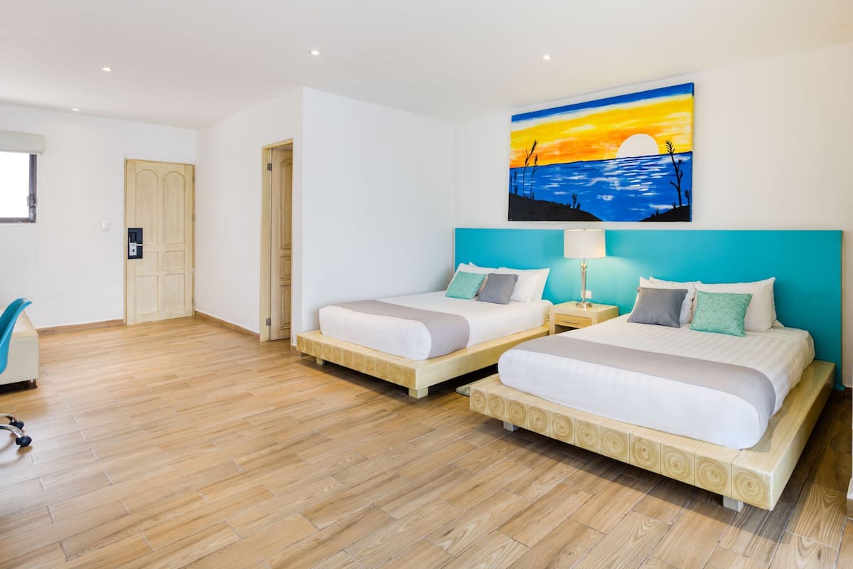 Quarto de hotel com duas camas, uma pintura de um pôr do sol e piso de madeira.