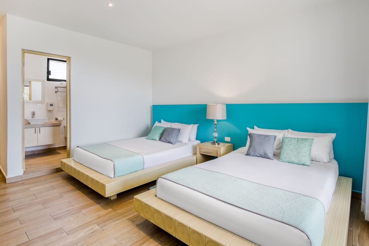Quarto de hotel com duas camas, banheiro e vista para o exterior.