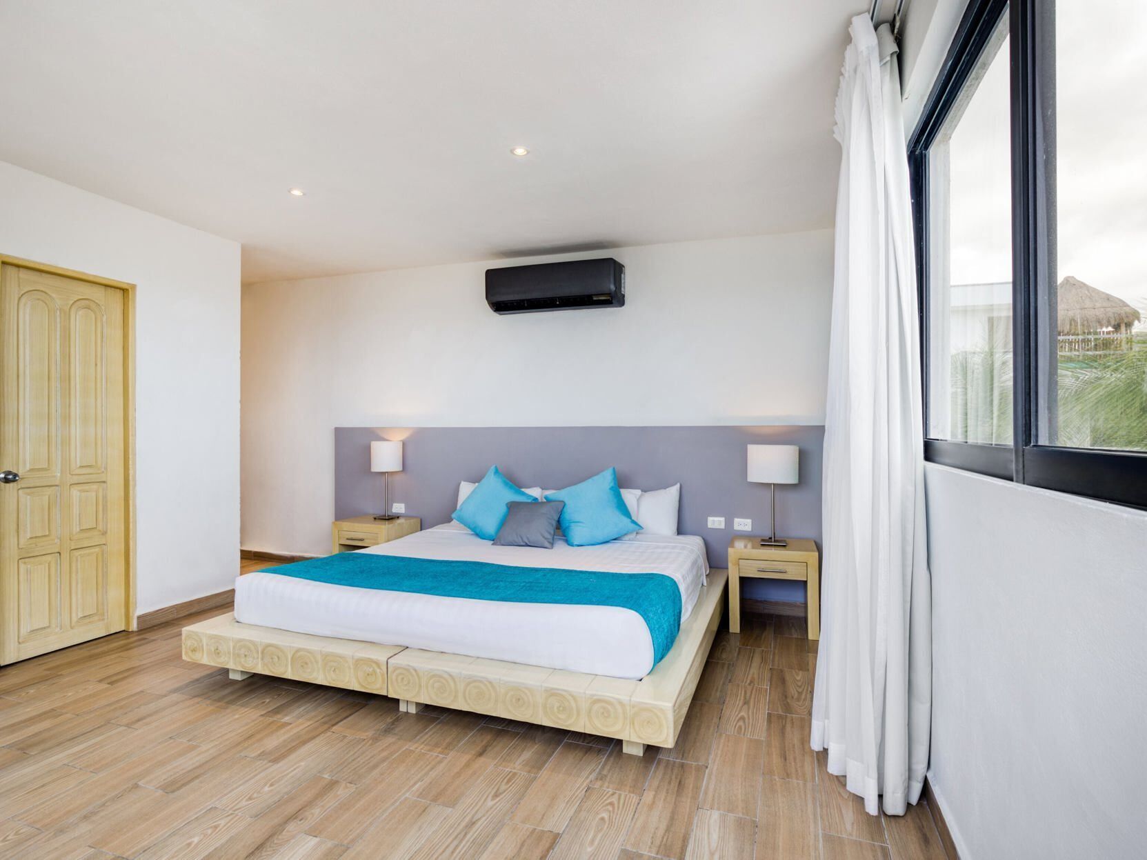 Quarto com cama, duas mesas de cabeceira, janela e aparelho de ar condicionado.