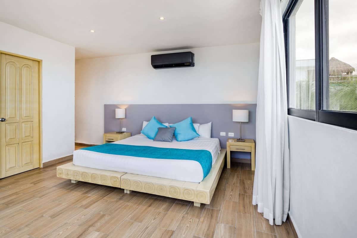 Quarto com cama, duas mesas de cabeceira, janela e aparelho de ar condicionado.