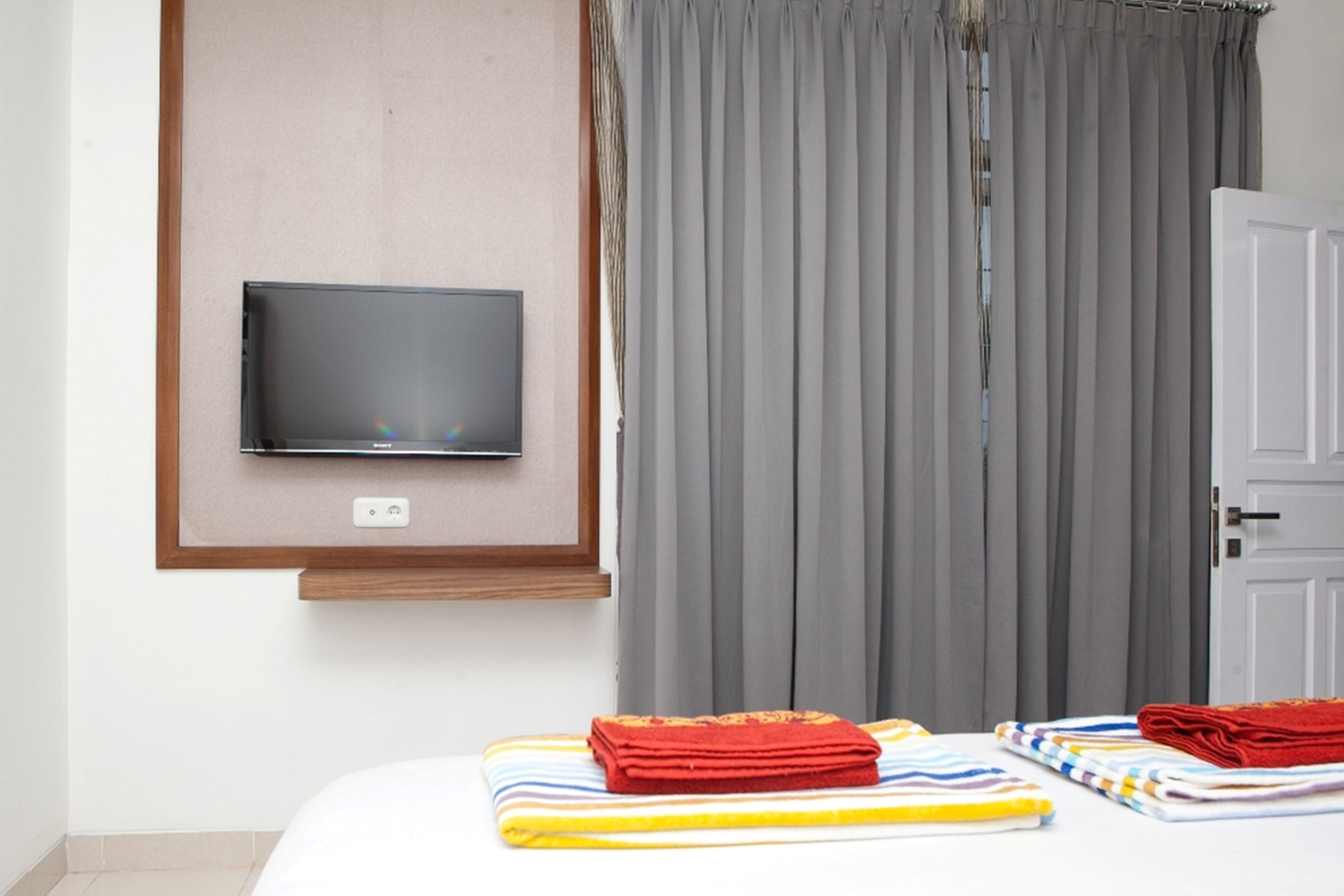 Quarto de hotel com cama, televisão na parede e uma porta.