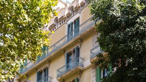 Um edifício de vários andares com varandas, persianas verdes e estilo arquitetônico clássico.