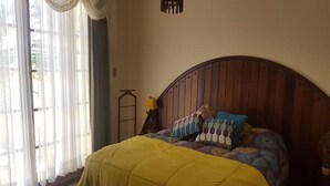 Quarto com cama, um banco e janela com cortinas.
