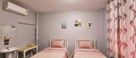 Quarto com duas camas, uma mesinha de cabeceira, um espelho, uma pia e ar-condicionado fixado na parede.
