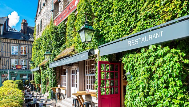 Um restaurante com mesas ao ar livre, uma porta vermelha e paredes cobertas de hera.