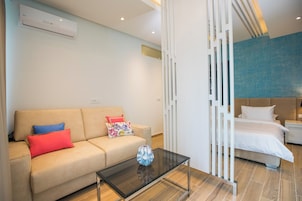 Quarto de hotel moderno com sofá, mesa de centro de vidro e cama.