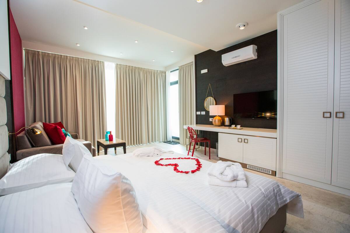 Quarto de hotel com cama grande, escrivaninha, cadeira, televisão e guarda-roupa.