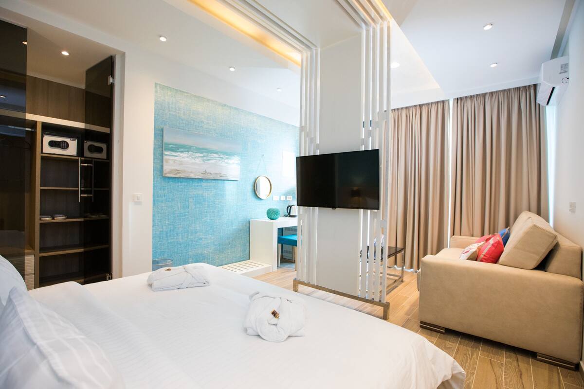 Quarto de hotel com cama, televisão, sofá e área de banheiro.