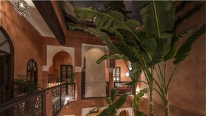 Um interior em vários níveis, com portas arqueadas, escadaria com grades elaboradas e plantas verdes grandes.