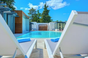 Uma área de piscina com espreguiçadeiras, um muro de madeira e um edifício de vidro ao fundo.
