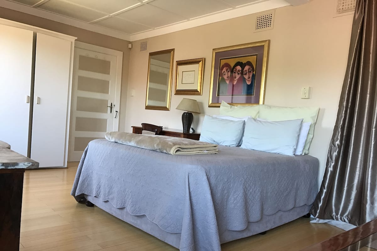 Uma cama bem arrumada com um cobre-leito azul claro, uma mesa de cabeceira com uma luminária e um quadro emoldurado sobre a cama.