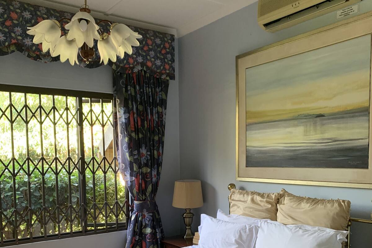 Um quarto com uma cama grande, um lustre pendurado, um quadro na parede e um aparelho de ar condicionado.
