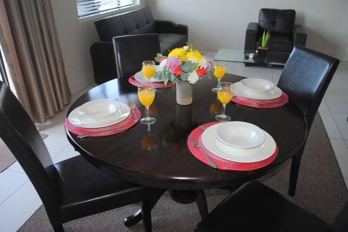Mesa de jantar posta com pratos, copos e um vaso de flores.