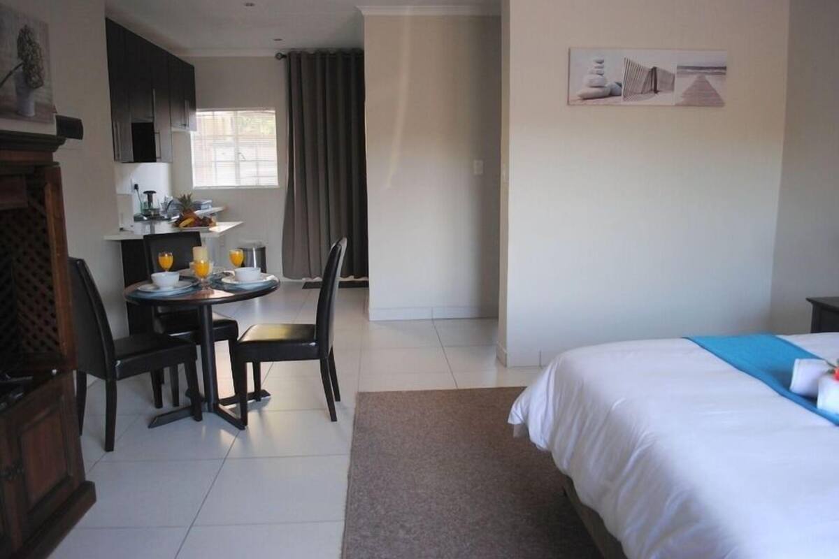 Quarto de hotel com cama, escrivaninha com cadeira, mesinha com bebidas e janela com cortinas.