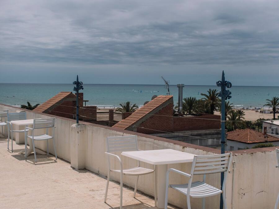 Terraço no telhado com cadeiras e mesas brancas, com vista para uma praia e o mar.