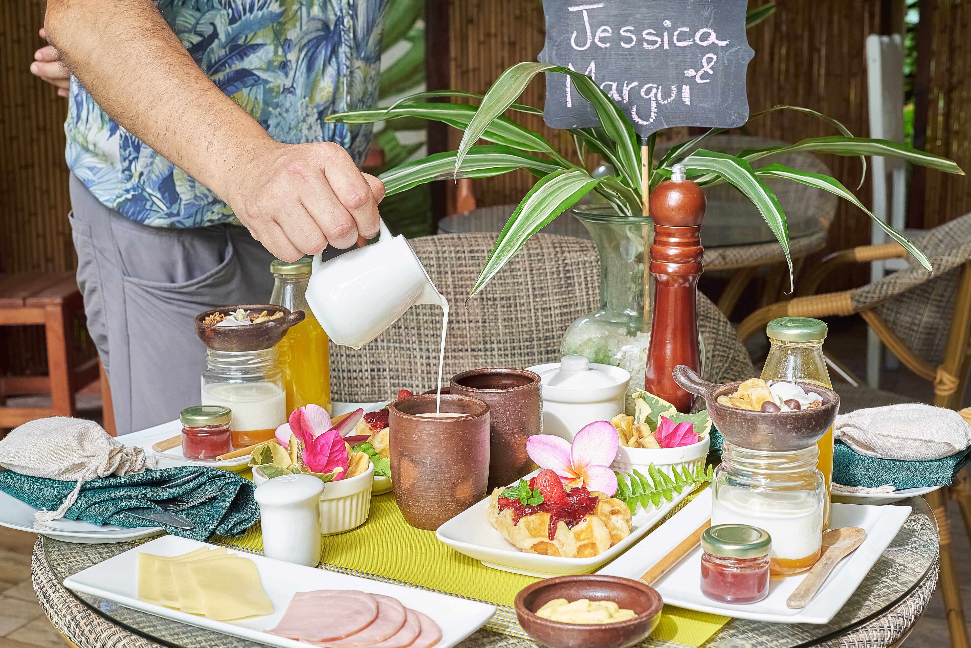 Uma mesa com diversos alimentos e uma pessoa servindo um líquido.
