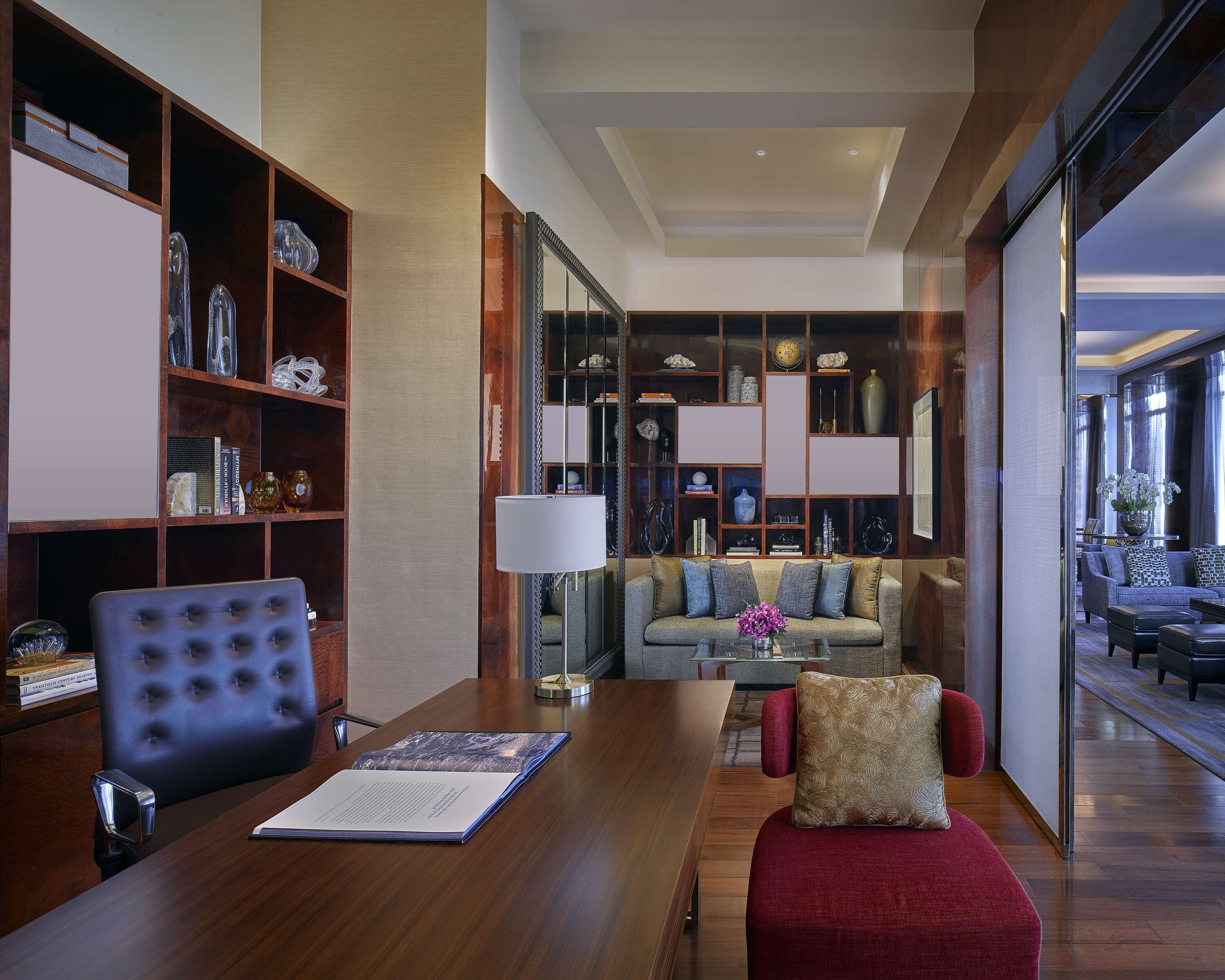 Uma sala de estar moderna com uma escrivaninha de madeira, uma poltrona de couro, um sofá e uma estante repleta de objetos decorativos.