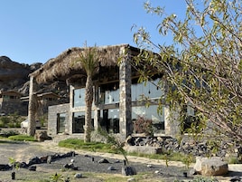 Um edifício de pedra com telhado de palha, área de recepção e vista para a paisagem ao redor.