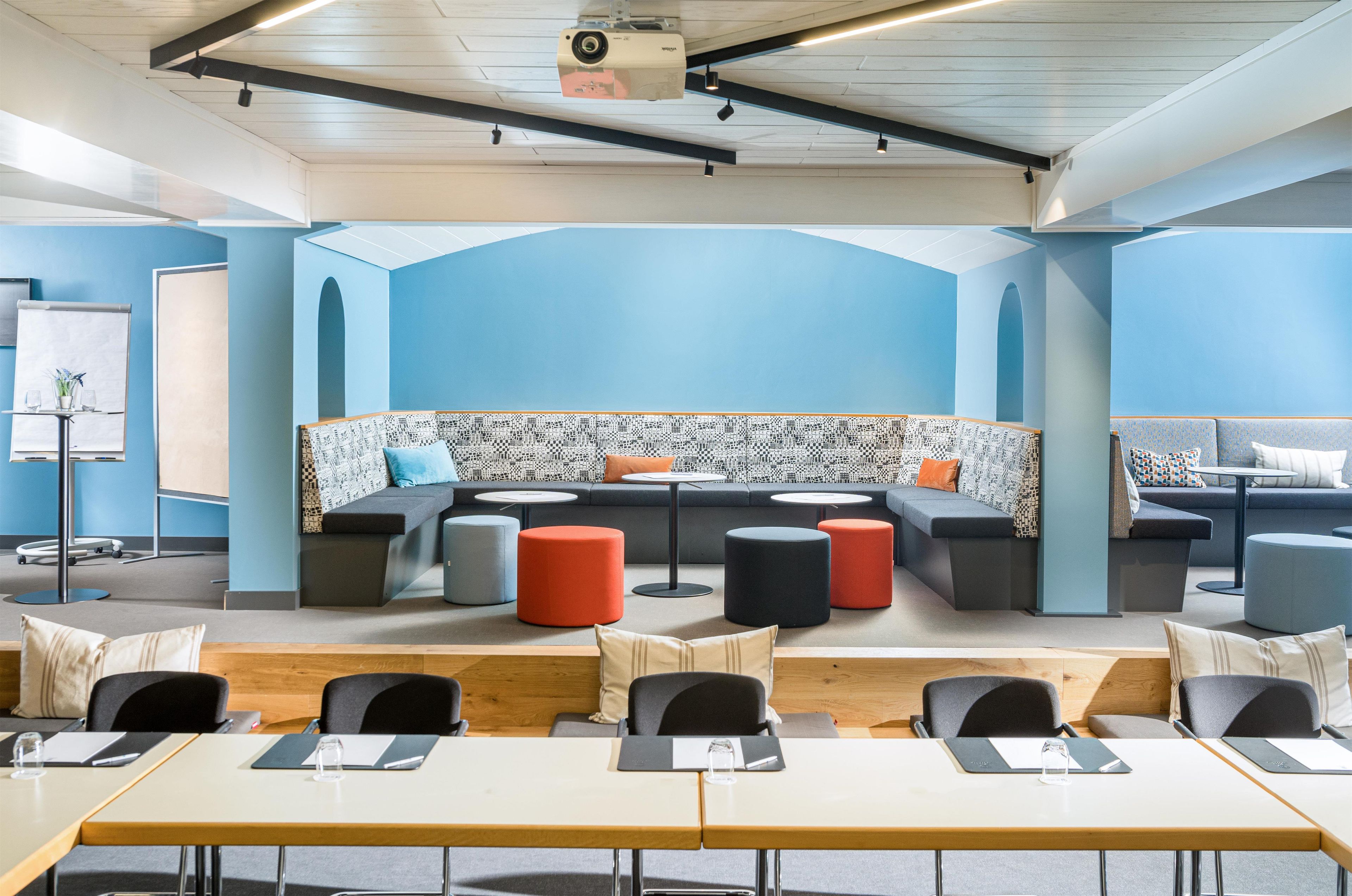 Uma sala de conferências moderna com tela grande, disposição de assentos e área para apresentações.