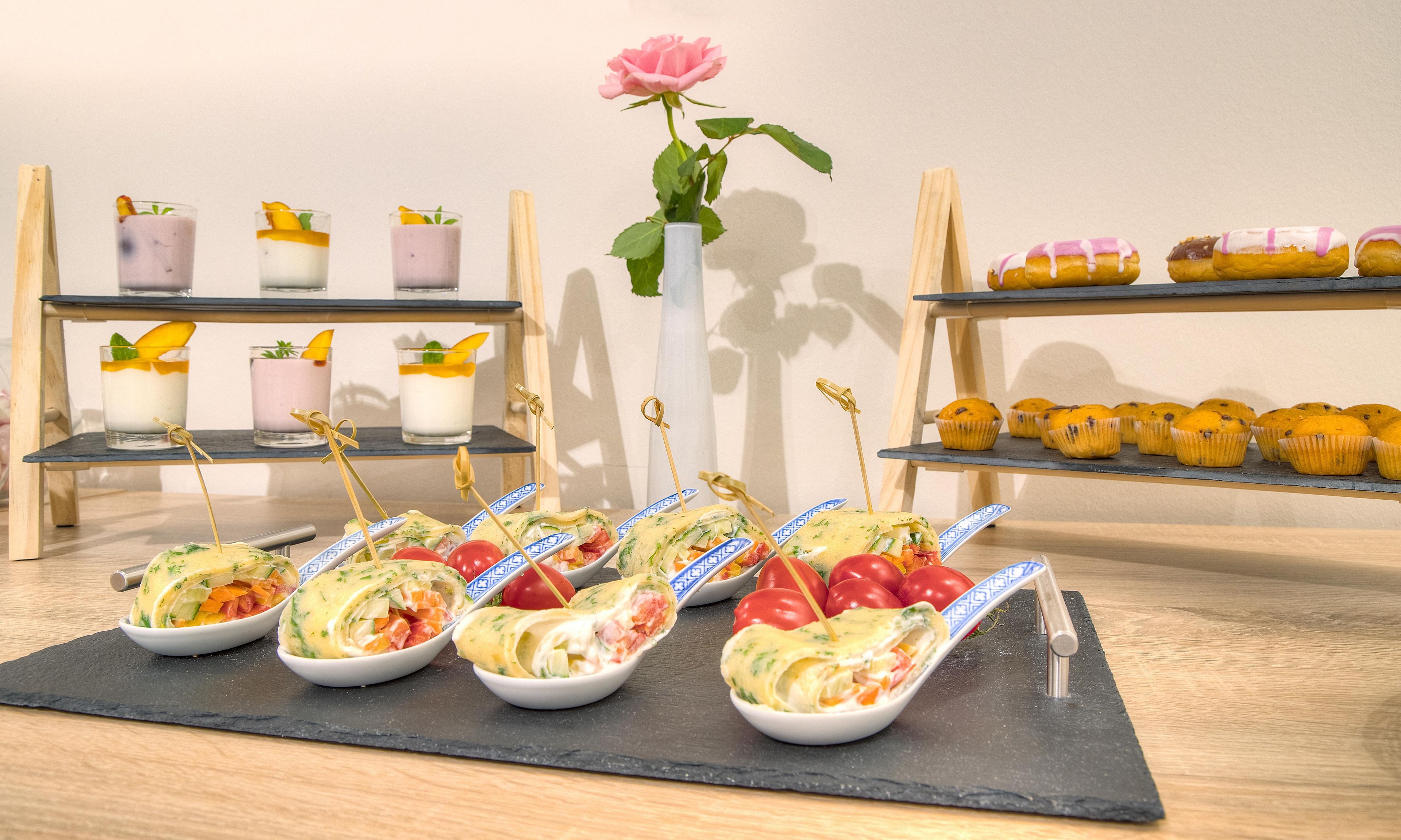 Diversos alimentos expostos numa mesa, com uma rosa num vaso.