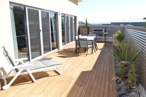 Um deck com mesa e cadeiras, uma poltrona de descanso e um vaso de planta.