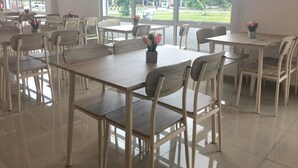 Uma ampla área de jantar com várias mesas e cadeiras, janelas grandes com vista para o exterior, e um design moderno e impecável.