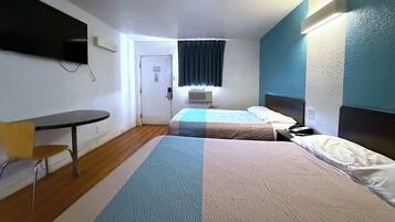 Quarto de hotel com cama, uma cadeira, uma mesa, TV fixada na parede e janela com cortinas.