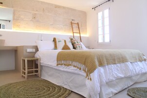 Quarto com uma cama grande, uma escada de madeira, um banquinho pequeno e um tapete tecido.