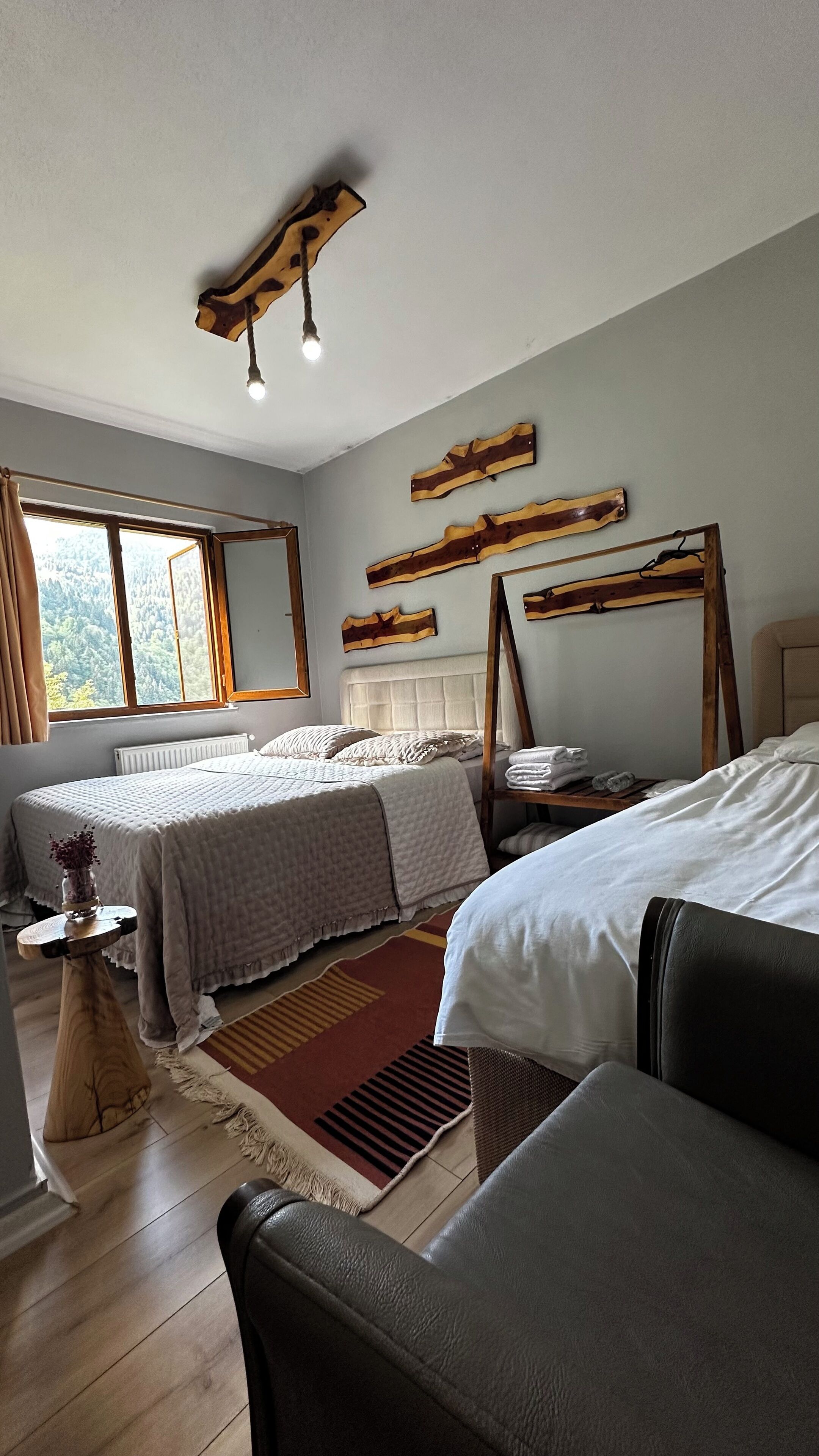 Quarto com duas camas, uma cabeceira de madeira, uma peça de arte na parede em madeira, uma janela com cortinas e piso de madeira.