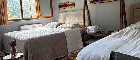 Quarto com duas camas, uma cabeceira de madeira, uma peça de arte na parede em madeira, uma janela com cortinas e piso de madeira.