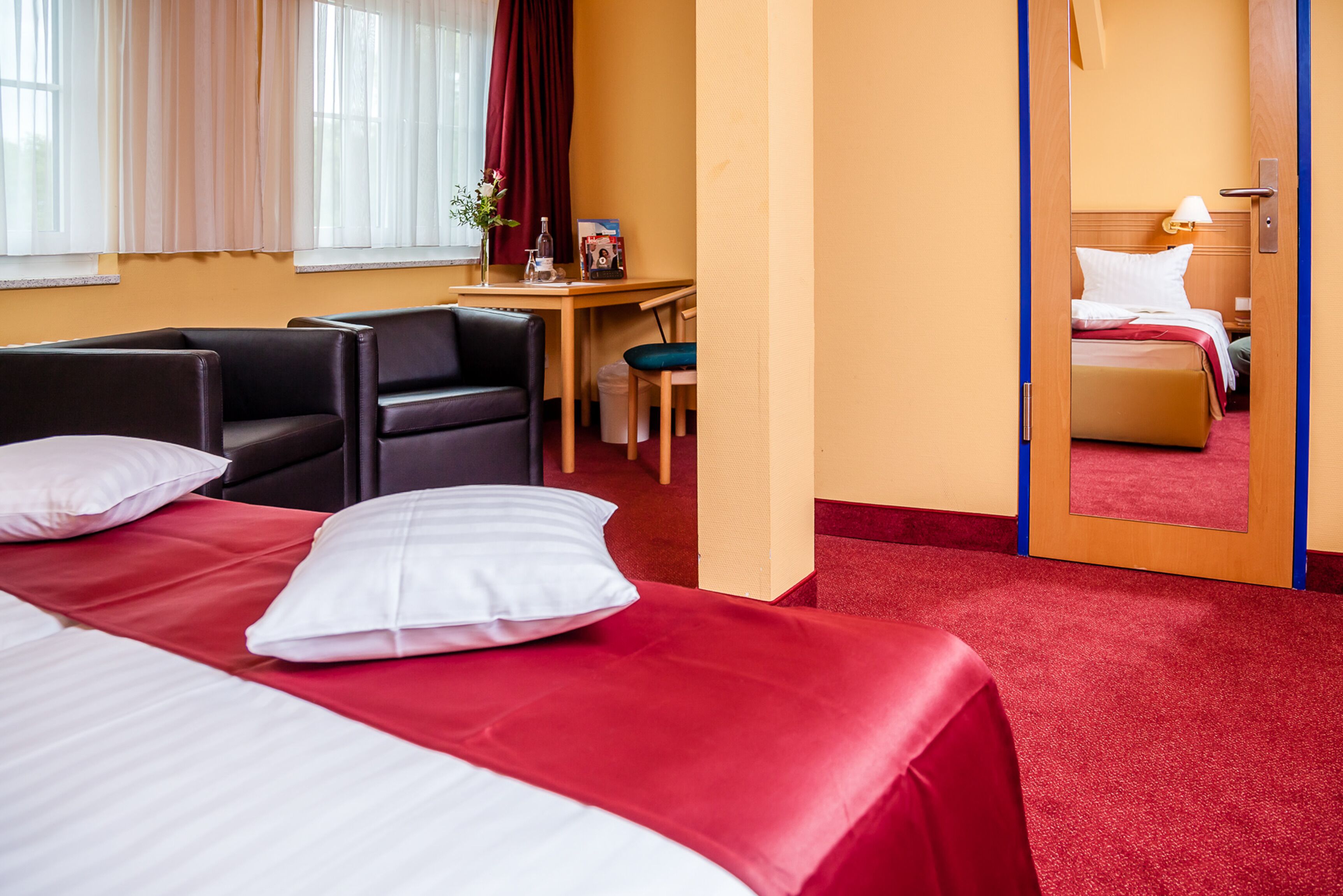 Quarto de hotel com uma cama, uma escrivaninha, uma cadeira e um espelho.
