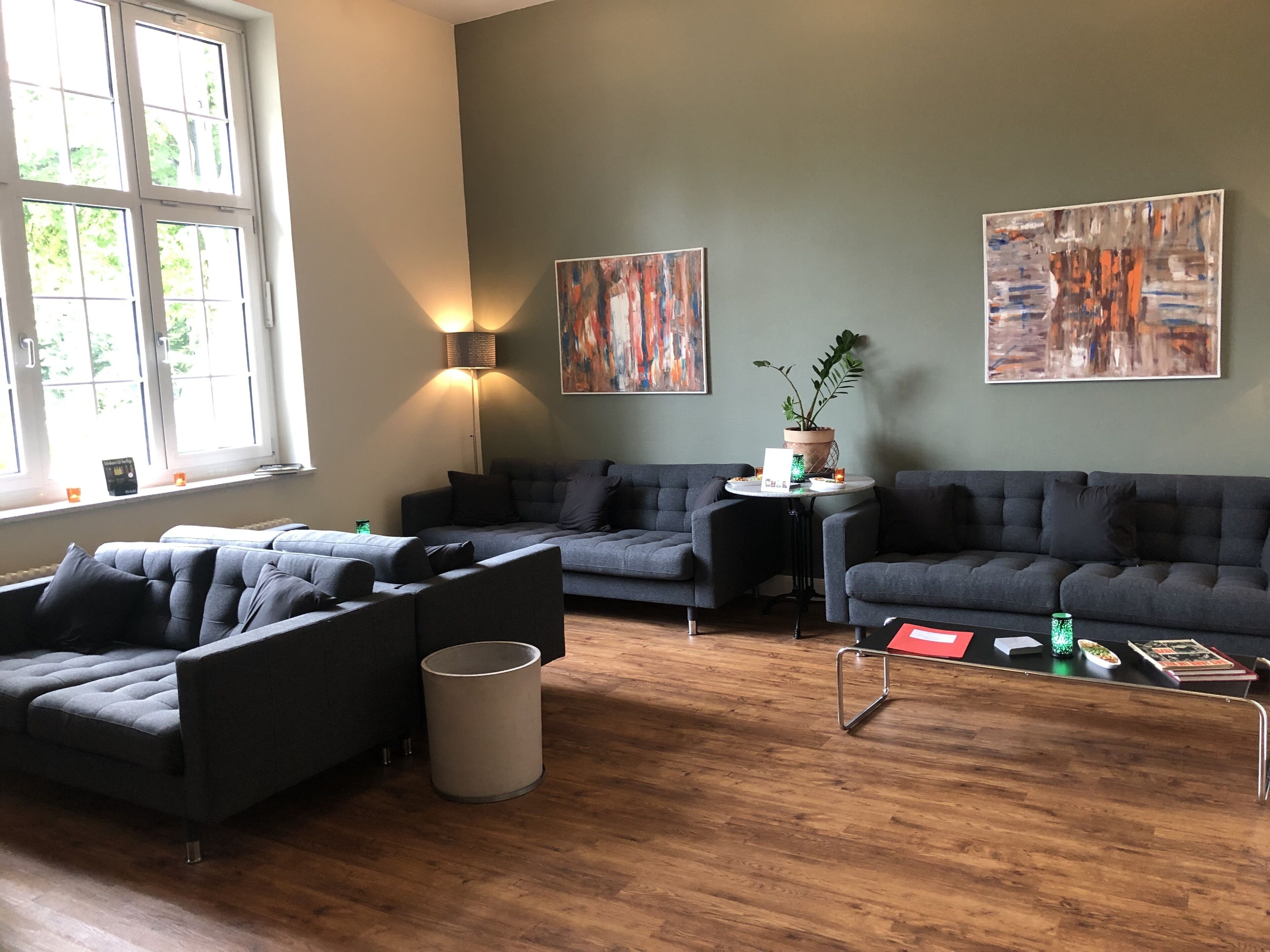 Uma sala de estar moderna com sofás cinza, piso de madeira e duas pinturas abstratas na parede.