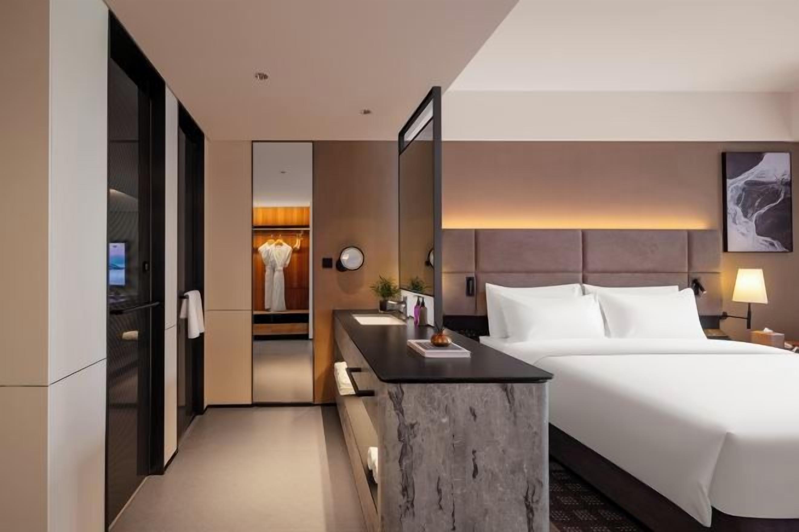 Quarto de hotel moderno com cama, mesa de cabeceira e espelho.
