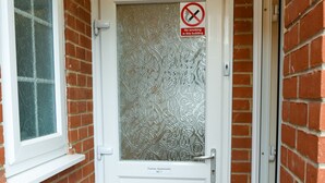 Uma porta branca com painel de vidro jateado e placa de proibido fumar.
