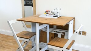 Um quarto pequeno com uma mesa de madeira e duas cadeiras brancas, um espelho e uma televisão na parede.