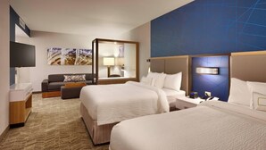 Quarto de hotel com duas camas, um sofá, uma televisão e um espelho grande.