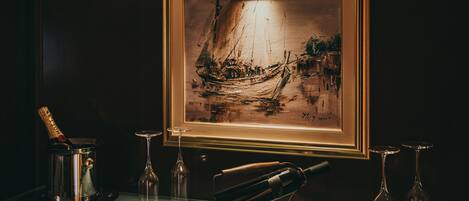 Um quadro emoldurado com um barco à vela, uma garrafa de champanhe e vários copos de vinho sobre uma mesa de vidro.