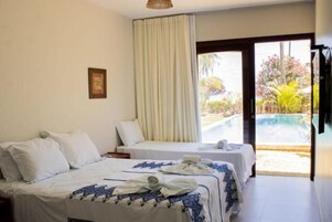 Quarto de hotel com duas camas, uma janela grande com vista para uma piscina e um jardim, e uma porta que dá para área externa.