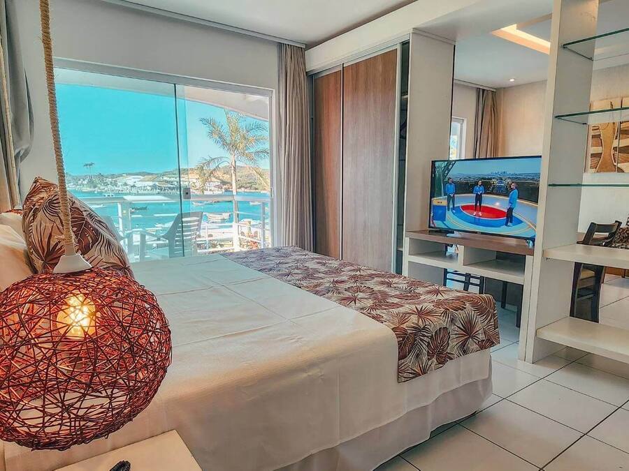 Quarto de hotel moderno com uma cama grande, televisão e vista para o mar.