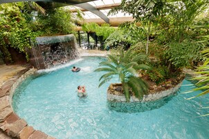 Piscina interior com cascata, rodeada por vegetação exuberante e paredes de pedra.