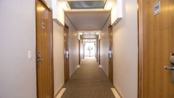 Corredor de hotel com portas de madeira, pisos cobertos por carpete e um claraboia.