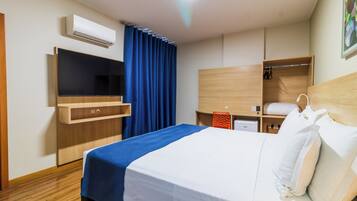 Quarto de hotel com cama, televisão, guarda-roupa, secretária e ar condicionado.