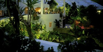 Um jardim interno com vários níveis, teto de vidro, paredes de pedra e vegetação exuberante.