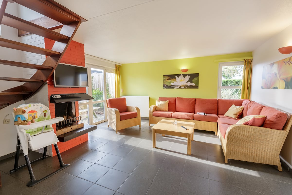 Uma sala de estar com escada de madeira, um sofá, uma televisão e uma lareira.
