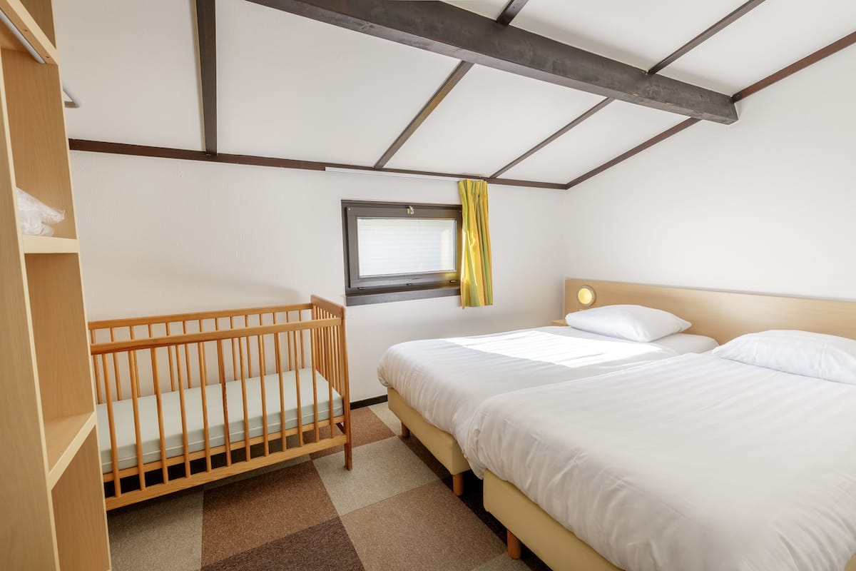 Quarto com berço, cama e janela com cortinas.